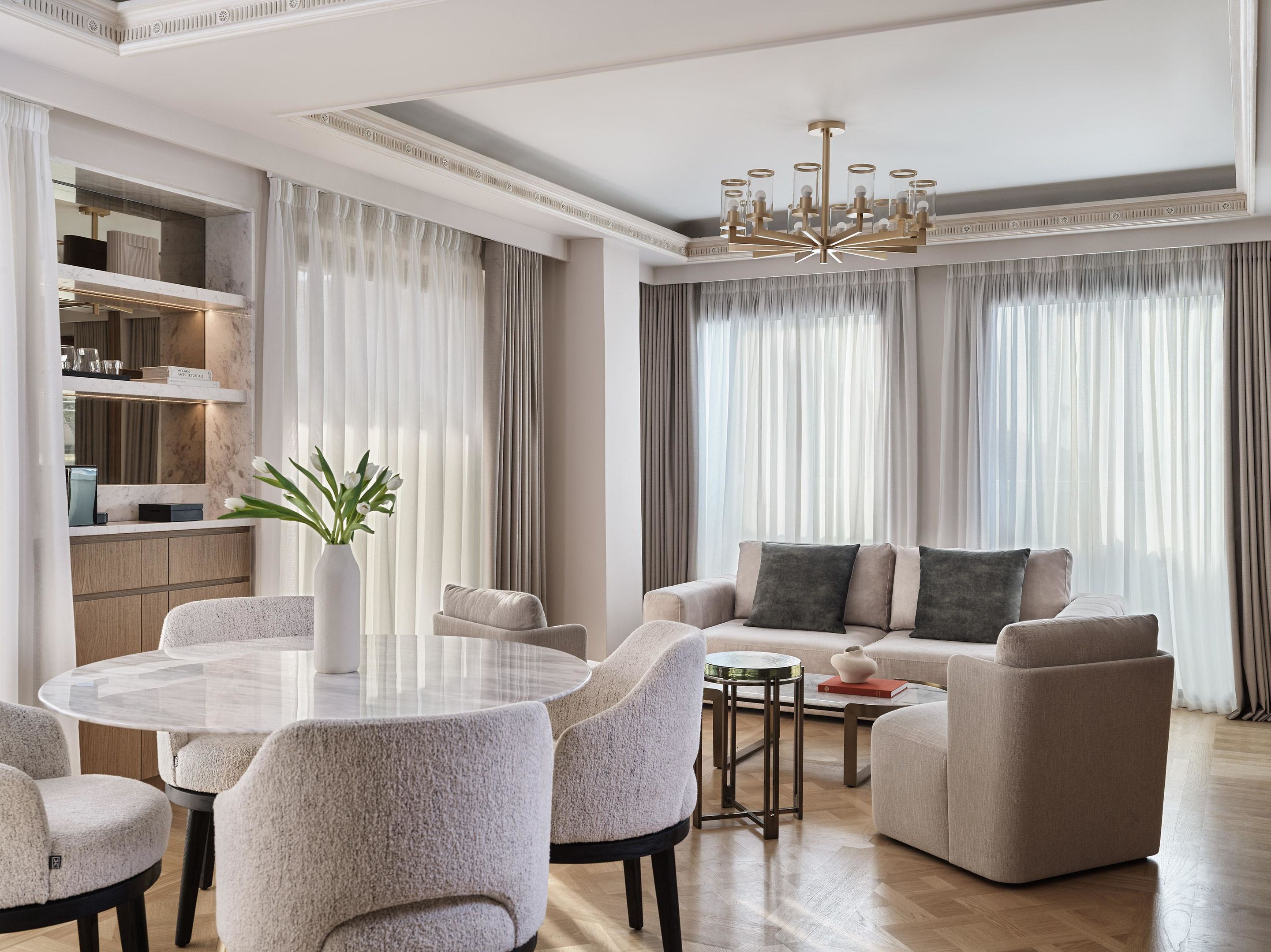Uma sala de estar moderna com uma mesa de jantar redonda, sofás confortáveis e um candelabro.