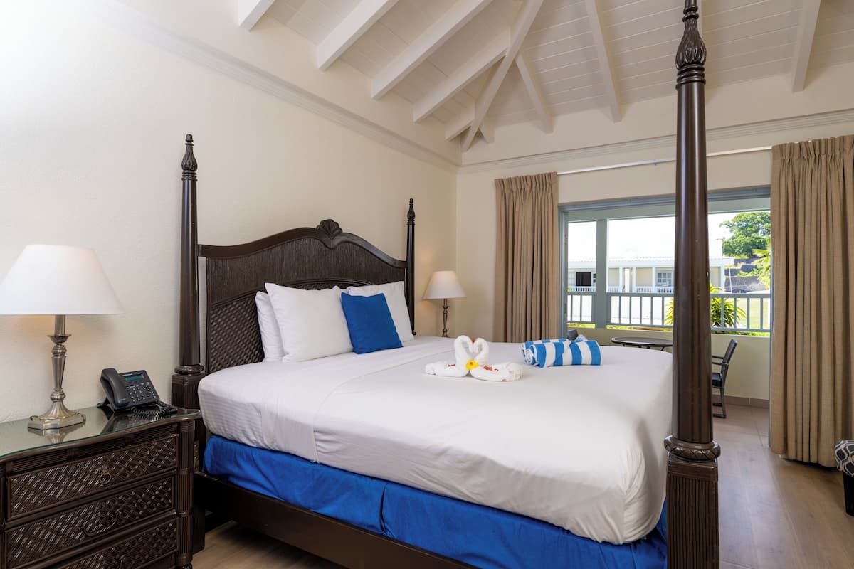 Uma cama com dossel, roupa de cama branca e azul, um telefone ao lado da cama e uma mesa de cabeceira com abajur.