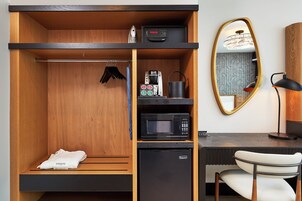 Quarto de hotel compacto com cozinha compacta, pequena geladeira, micro-ondas, cafeteira e espelho.