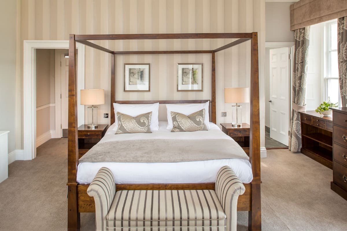 Uma cama com dossel e estrutura de madeira, duas mesas de cabeceira e um banco no pé da cama.
