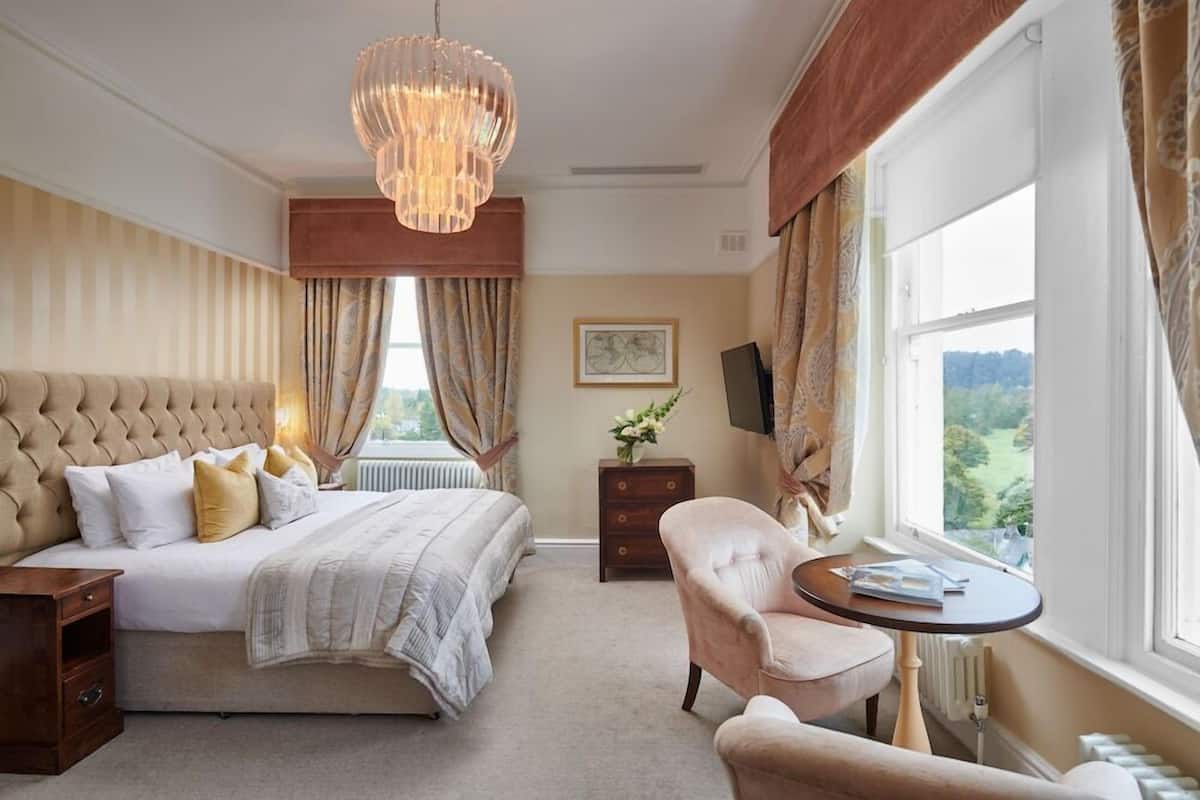 Quarto com uma cama grande, televisão, mesa pequena e janela com vista.