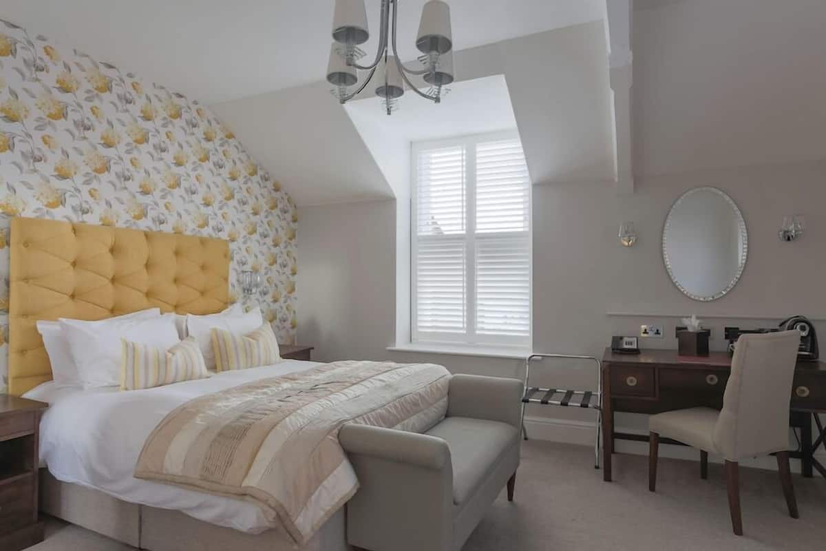 Quarto com cama, escrivaninha, cadeira, espelho e janela com persianas.