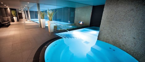 Uma área de piscina interior moderna com parede de vidro, espaço para sentar e parede de pedra.