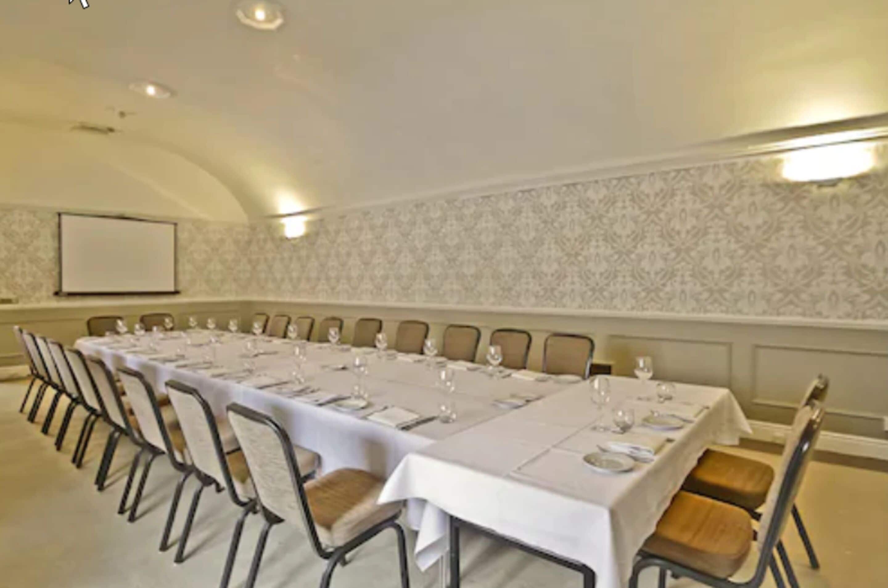 Uma sala de conferências com uma mesa comprida preparada para uma reunião, equipada com cadeiras e copos.