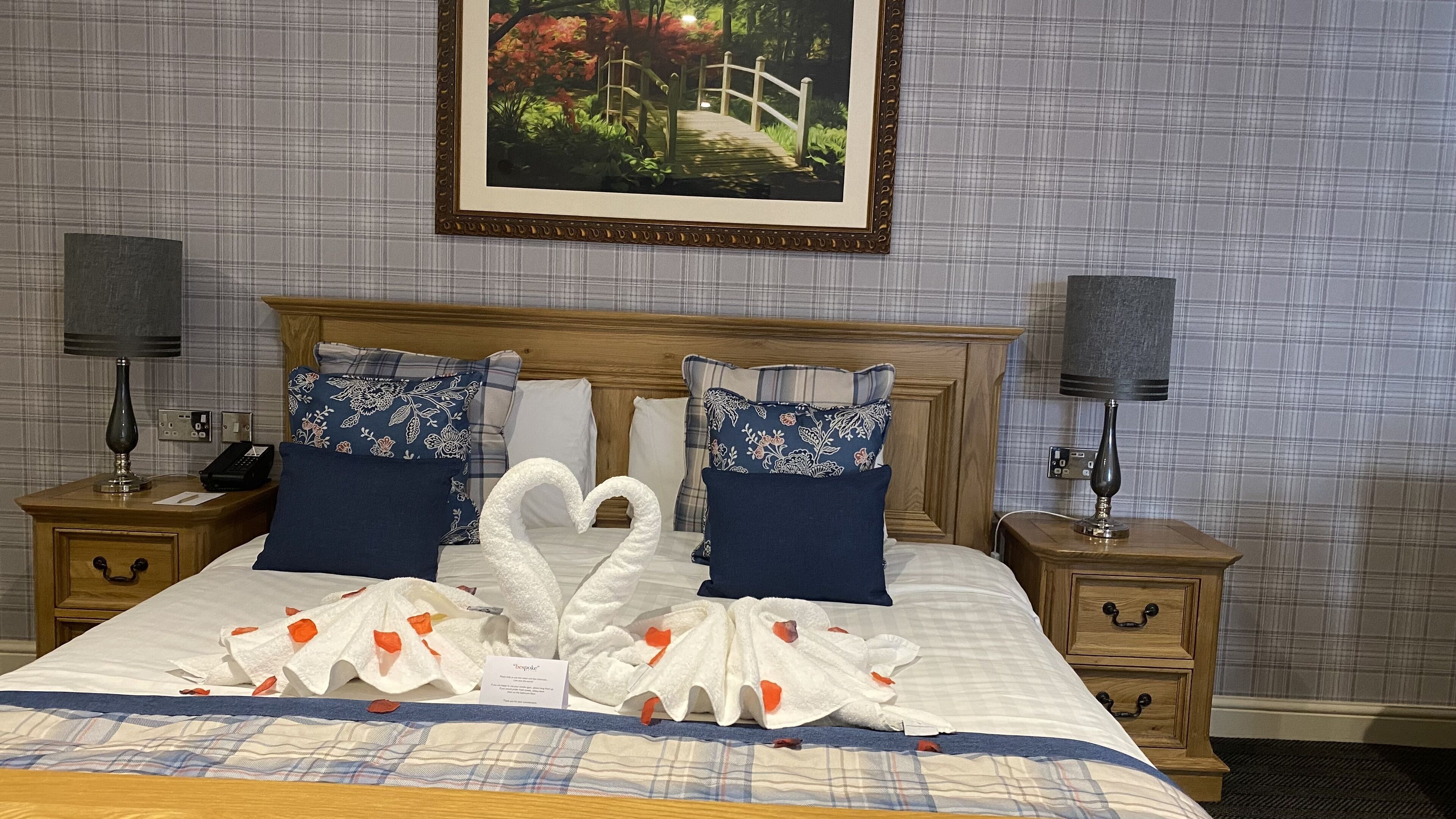 Uma cama bem arrumada com um edredom floral, dois travesseiros decorativos em formato de cisne e um quadro na parede.