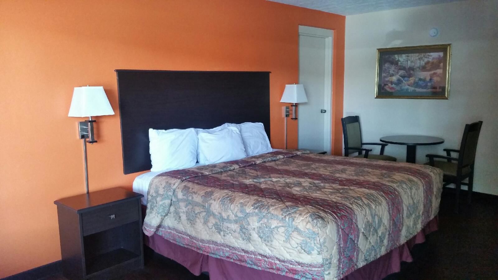 Quarto de hotel com uma cama grande, duas luminárias de cabeceira, uma mesinha e uma cadeira.
