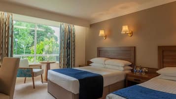 Quarto de hotel com duas camas, uma escrivaninha, uma cadeira e uma janela com cortinas.