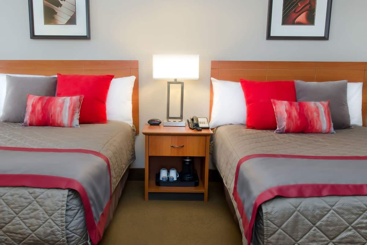 Quarto de hotel com duas camas, cada uma com cabeceira, mesa de cabeceira com abajur, telefone e gaveta.