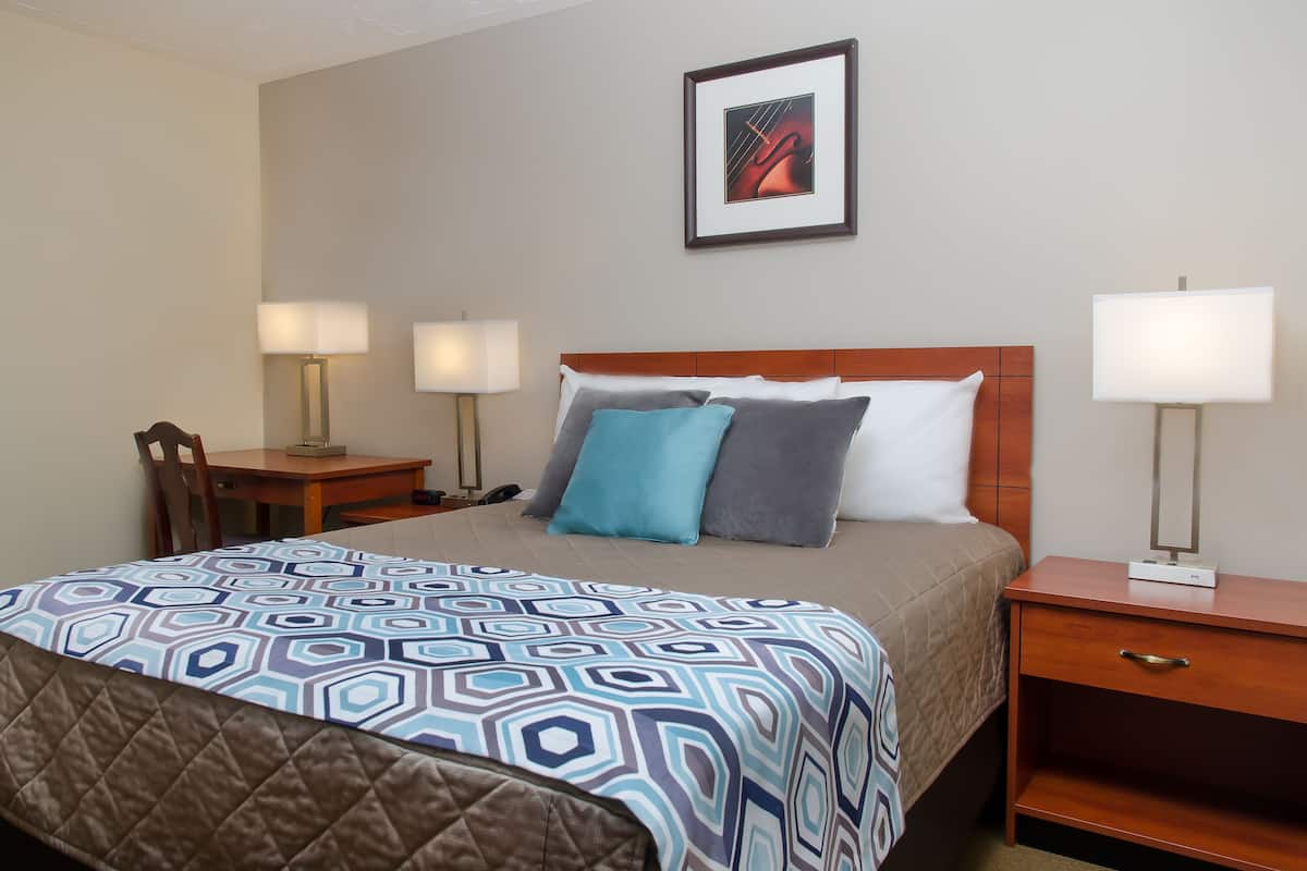 Quarto de hotel com cama, mesas de cabeceira, escrivaninha e uma cadeira.