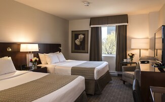 Quarto de hotel com duas camas, uma mesa, uma cadeira, uma televisão e uma janela com cortinas.