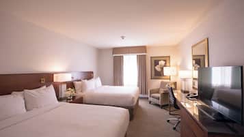 Quarto de hotel com duas camas, uma mesa de trabalho, uma televisão, uma cadeira e um abajur.