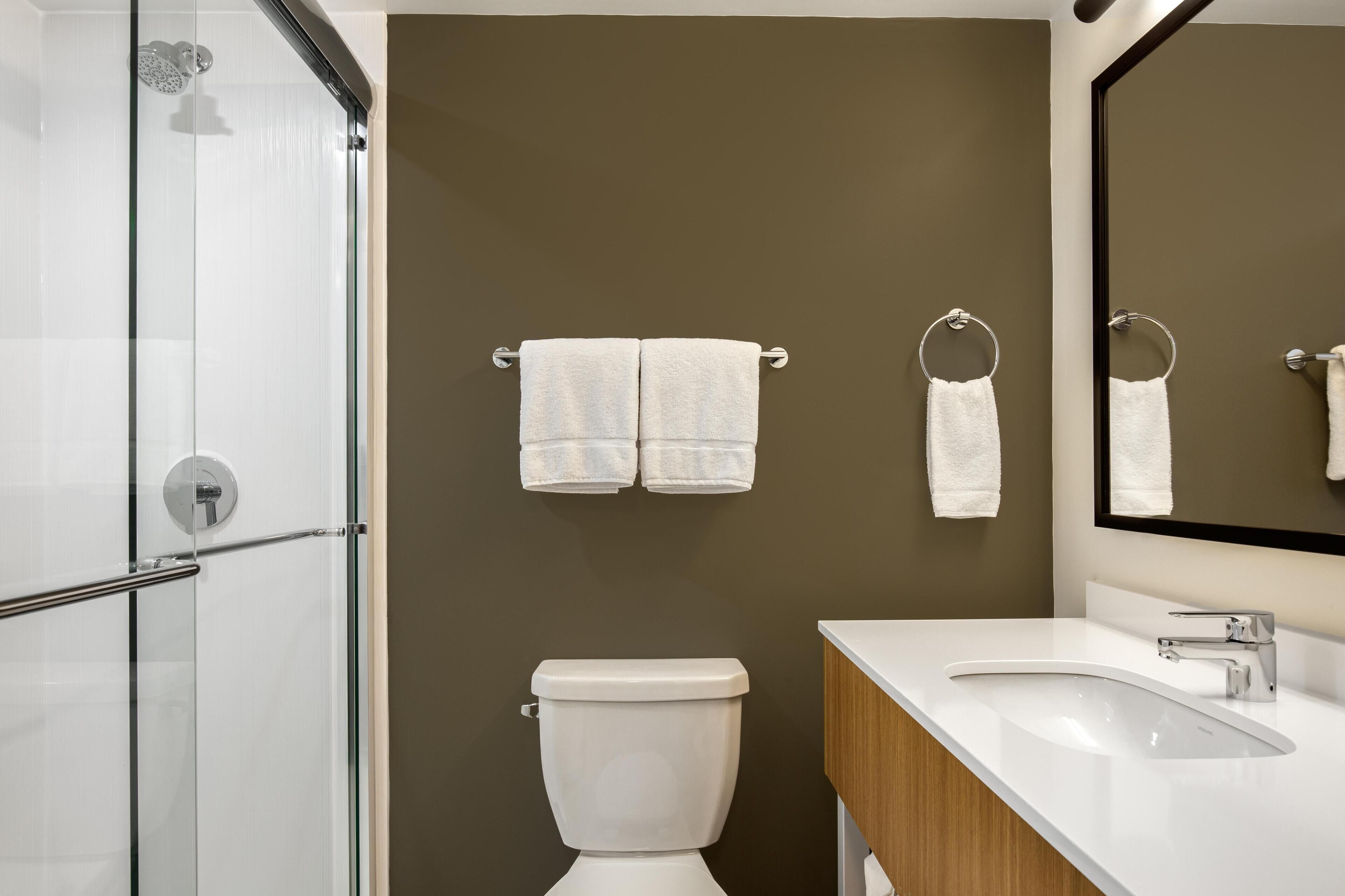 Um banheiro moderno com box de vidro, vaso sanitário branco e pia com armário de madeira.