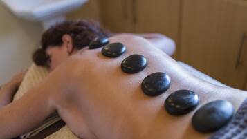 Uma pessoa recebendo uma massagem nas costas com pedras pretas colocadas sobre elas.