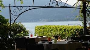Restaurante com área externa e mesas de frente para um lago, com taças de vinho e vista para a água.
