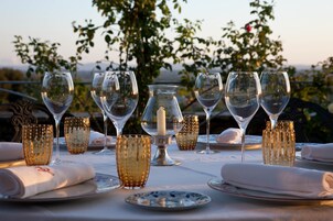 Mesa posta para refeição com taças de vinho, vela e copos decorativos.