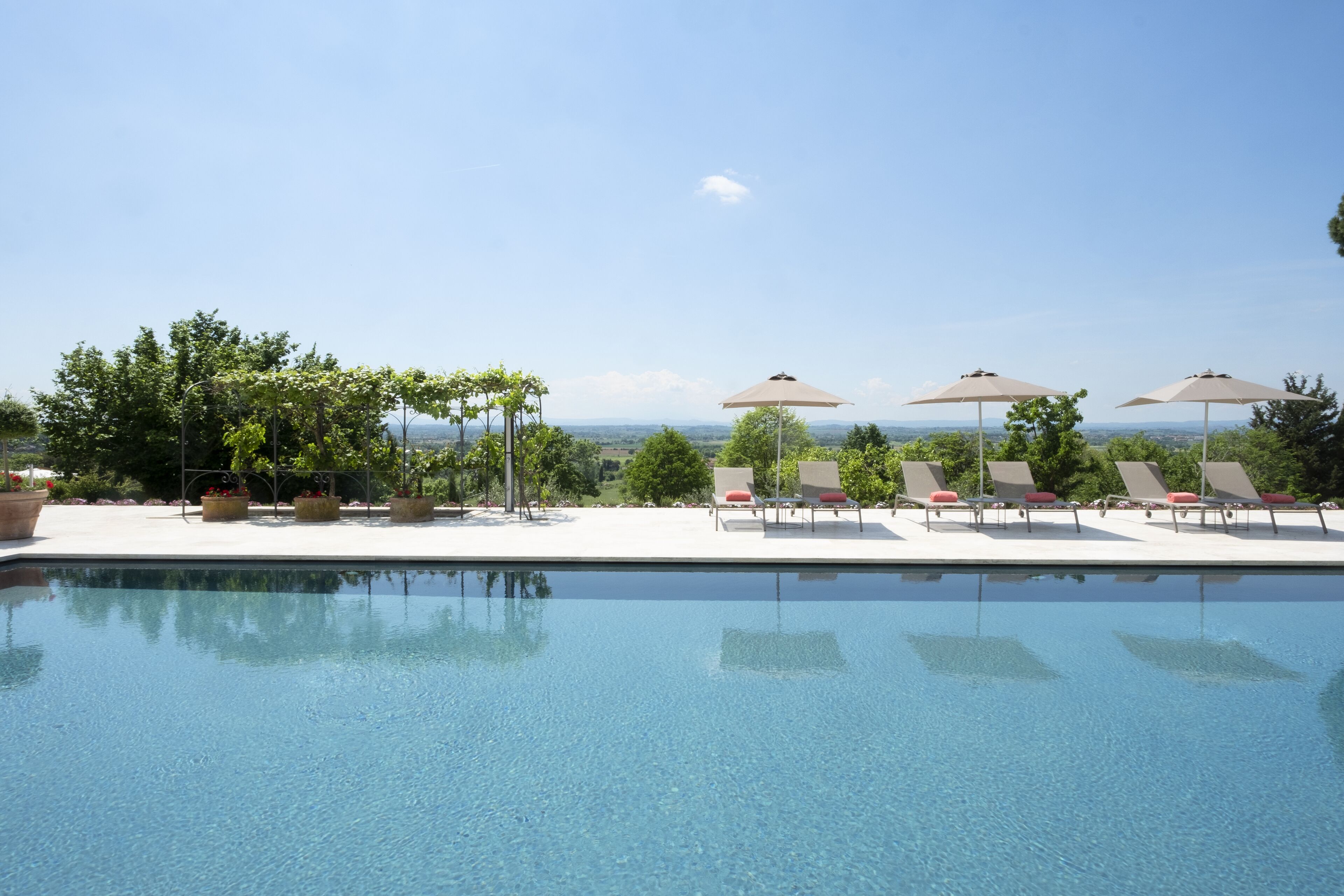 Piscina com espreguiçadeiras e guarda-sóis, cercada por árvores e um céu claro.