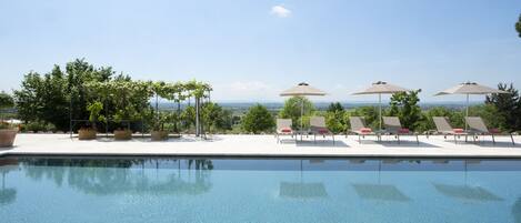 Piscina com espreguiçadeiras e guarda-sóis, cercada por árvores e um céu claro.