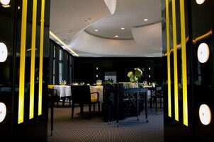 Uma área de jantar moderna com mesas preparadas para dois, com um arranjo floral central.