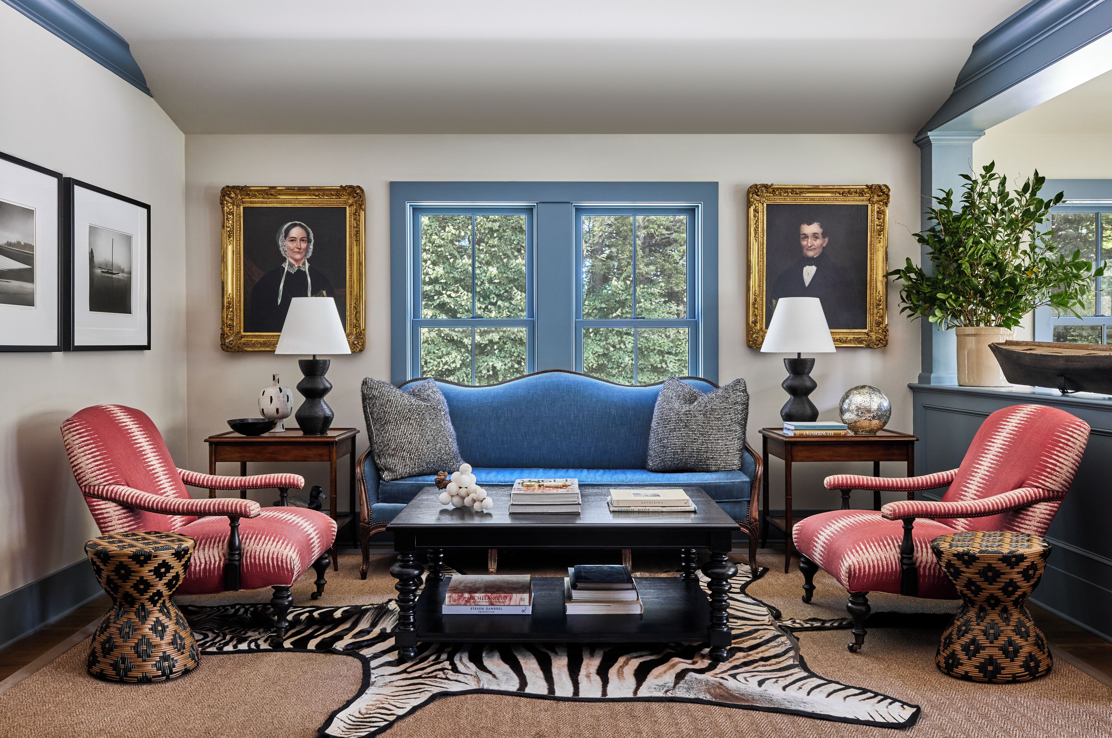 Um quarto com um sofá azul, duas poltronas vermelhas, uma mesa de centro preta e um tapete com padrão de zebra.