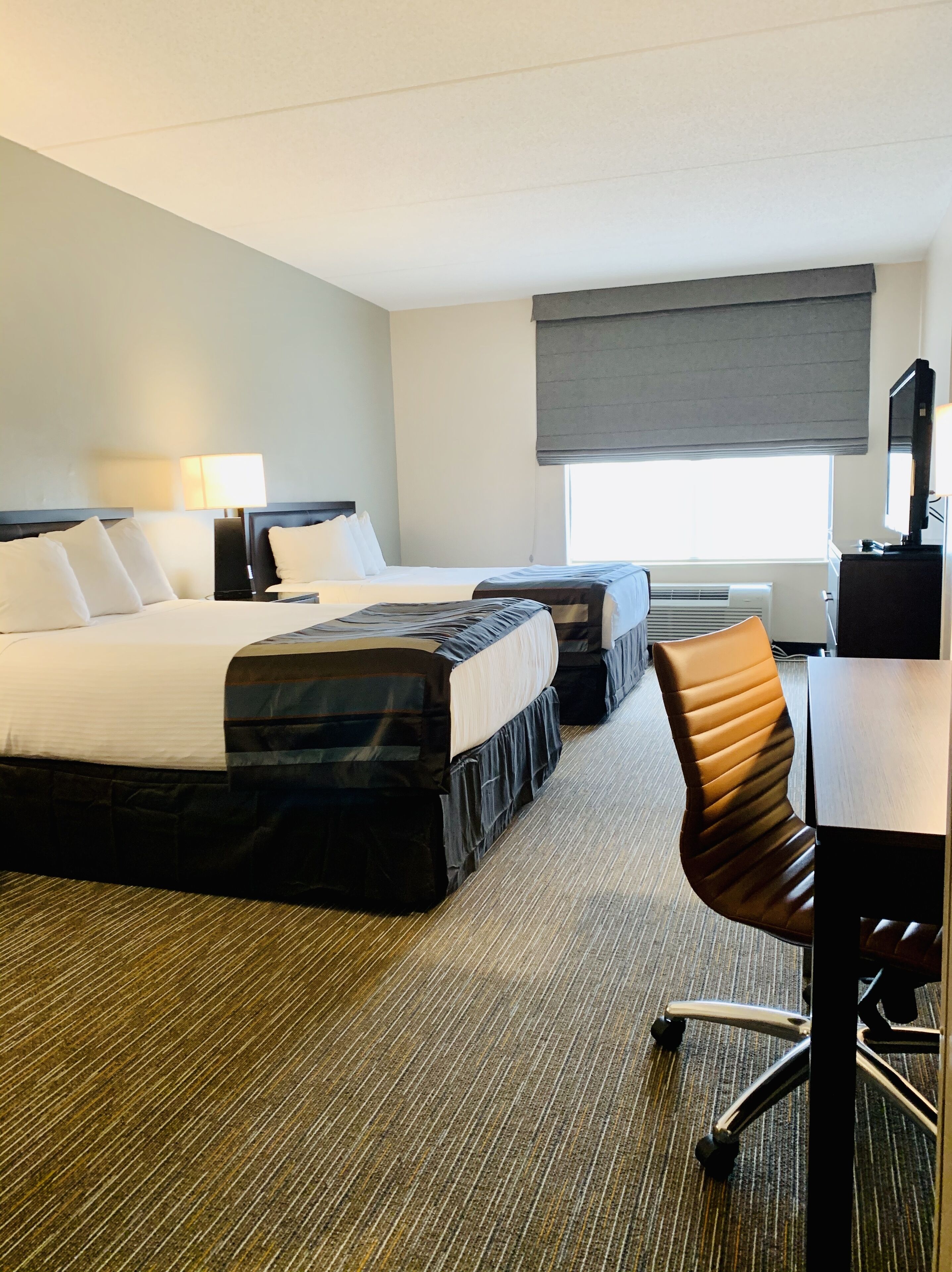 Quarto de hotel com duas camas, uma escrivaninha, uma cadeira, um abajur e uma televisão.