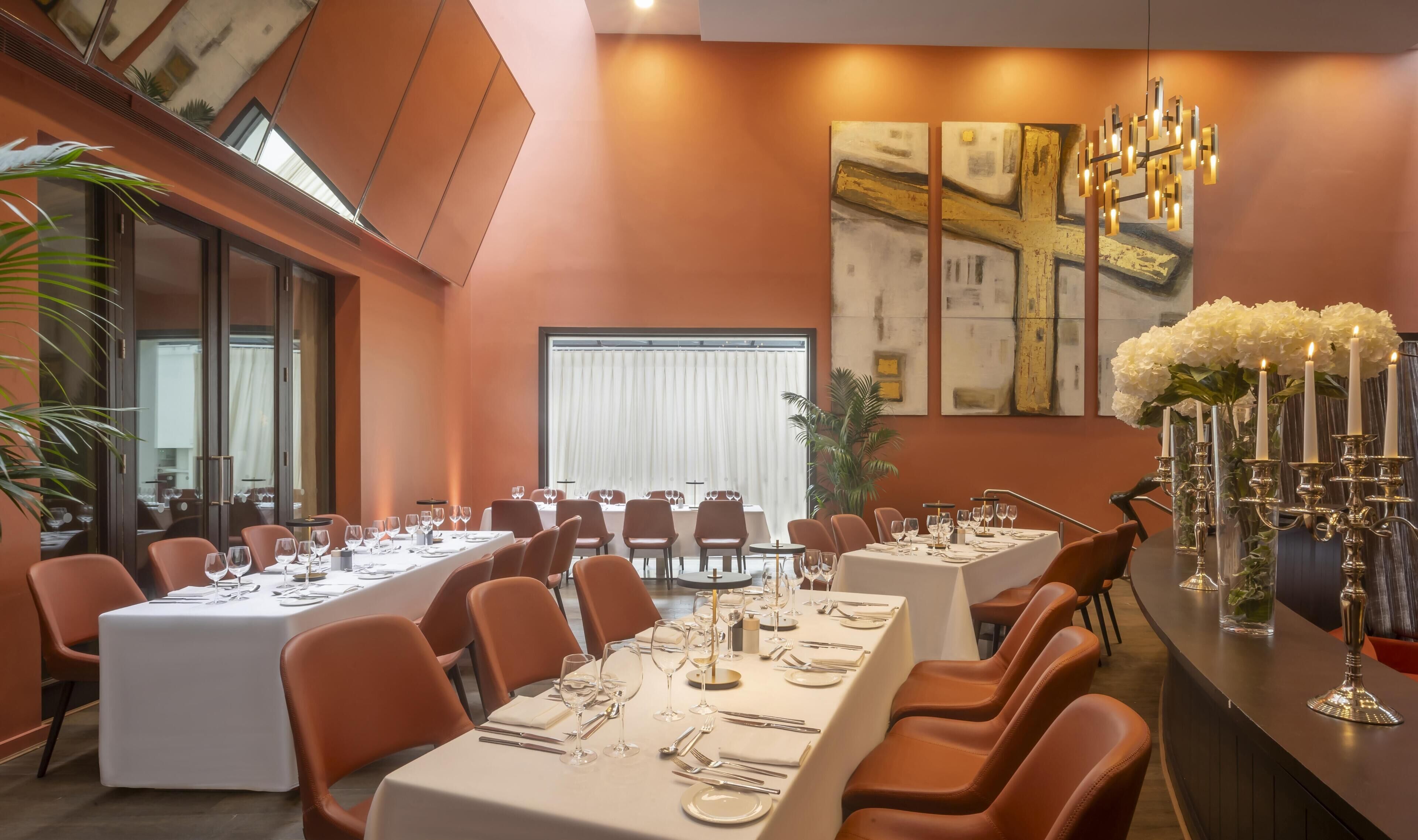 Uma sala de jantar com mesas grandes, cadeiras e um candelabro.