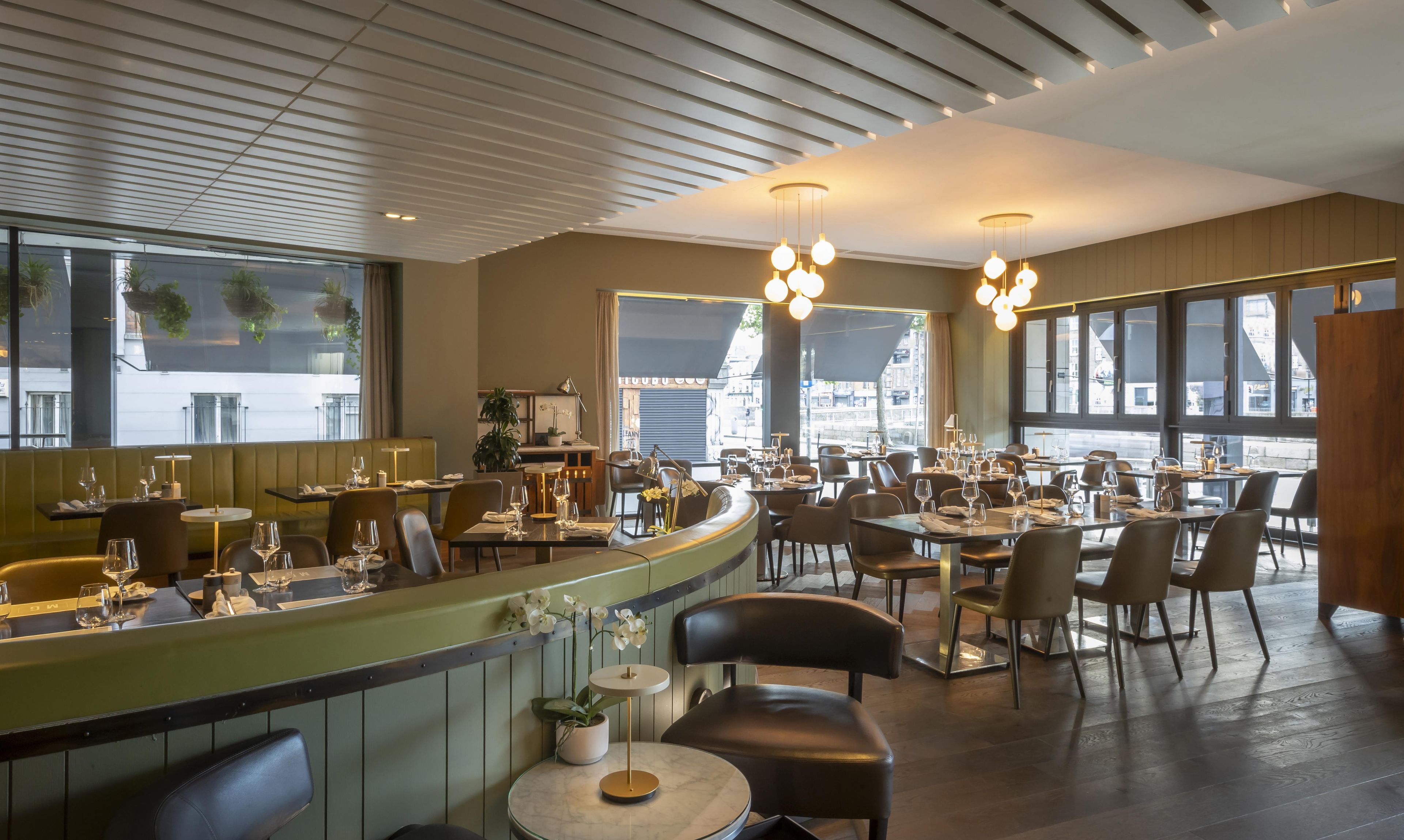Interior de restaurante com um balcão curvo, várias mesas para refeições e cadeiras.