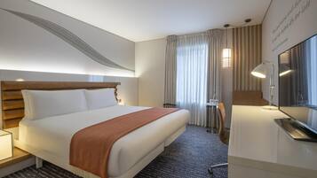 Quarto de hotel com cama, mesa de cabeceira, luminária e espelho.