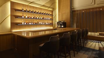 Uma área de bar com diversas prateleiras de garrafas, uma máquina de café e banquetas.
