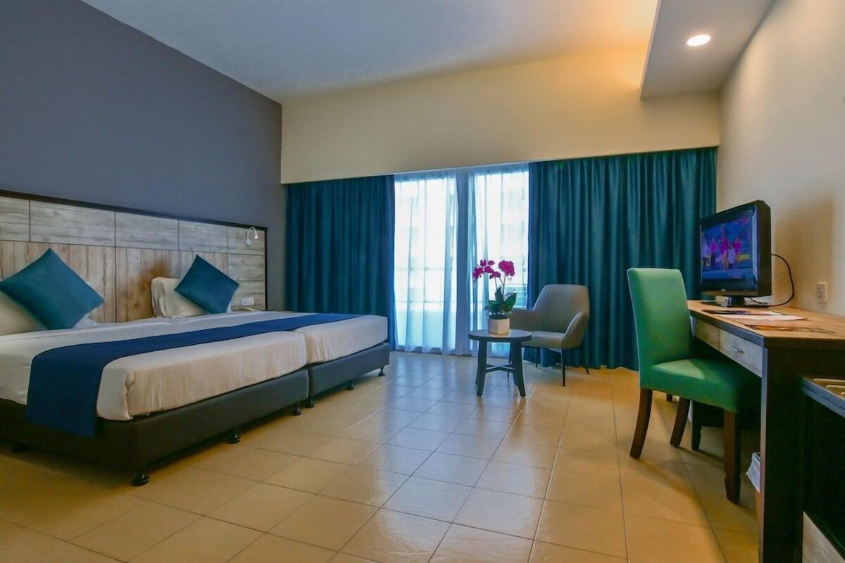 Quarto de hotel com cama de casal, escrivaninha com computador, cadeira e televisão.