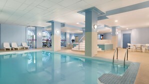 Piscina interna com água cristalina, rodeada por espreguiçadeiras e uma escadaria que leva a um andar superior.