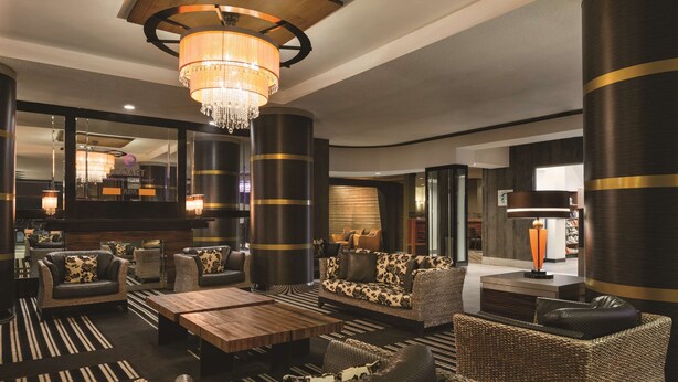 Um lobby moderno com um candelabro, sofás e uma mesa de centro de madeira.
