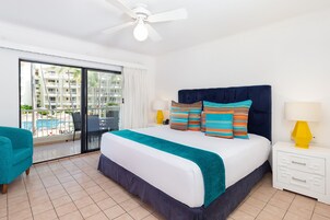 Quarto de hotel com cama, mesa de cabeceira, cadeira e vista para uma piscina e edifícios.
