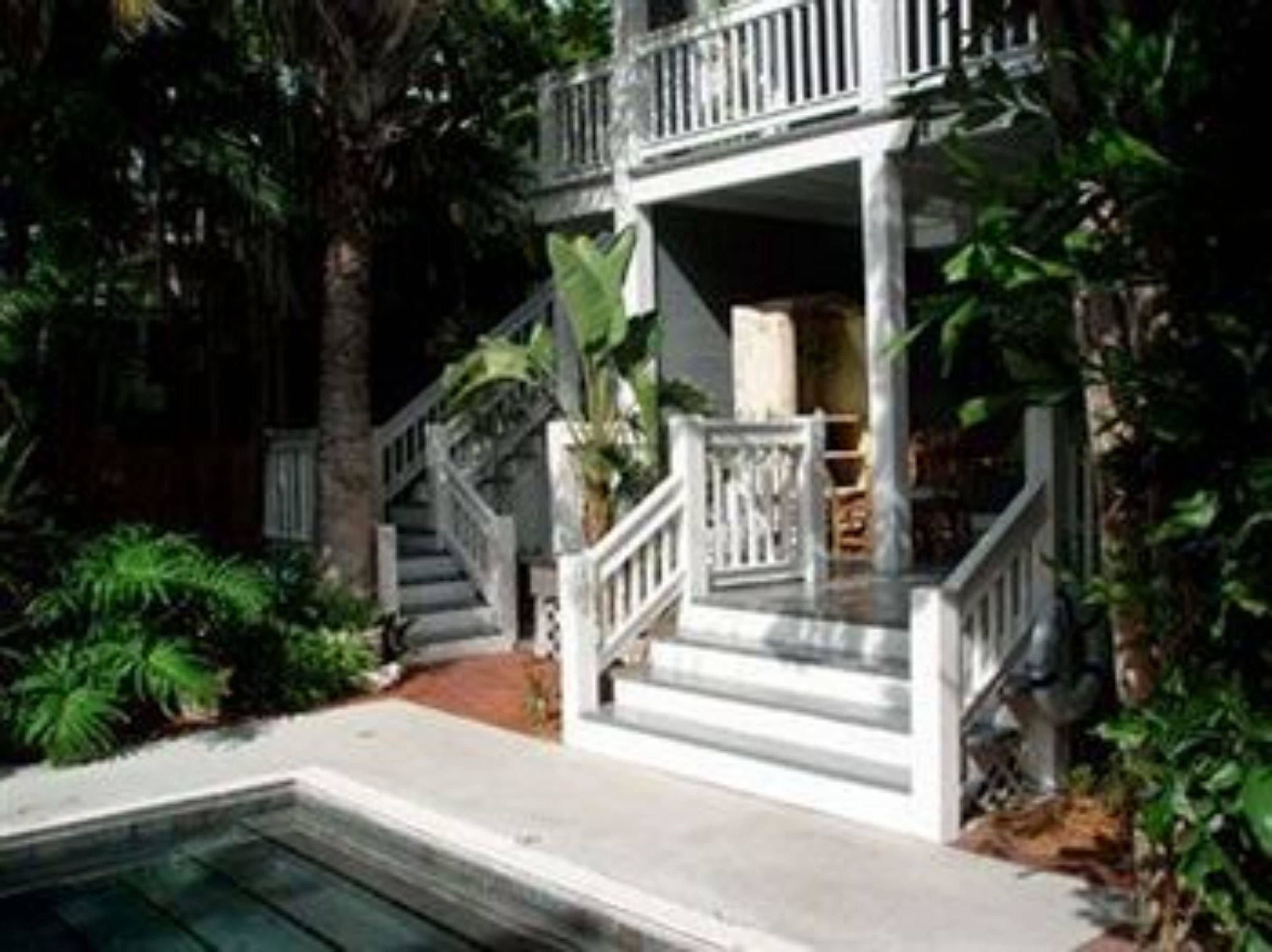 Um edifício de dois andares com fachada branca, uma escadaria que leva ao nível superior e uma área de piscina em primeiro plano.