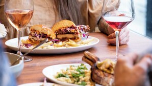 Uma mesa de jantar com um sanduíche, um copo de vinho e um prato de comida.