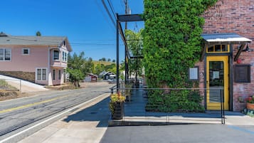 Uma plataforma de estação de trem com uma porta amarela, um prédio de tijolos coberto de hera e uma casa rosa ao fundo.