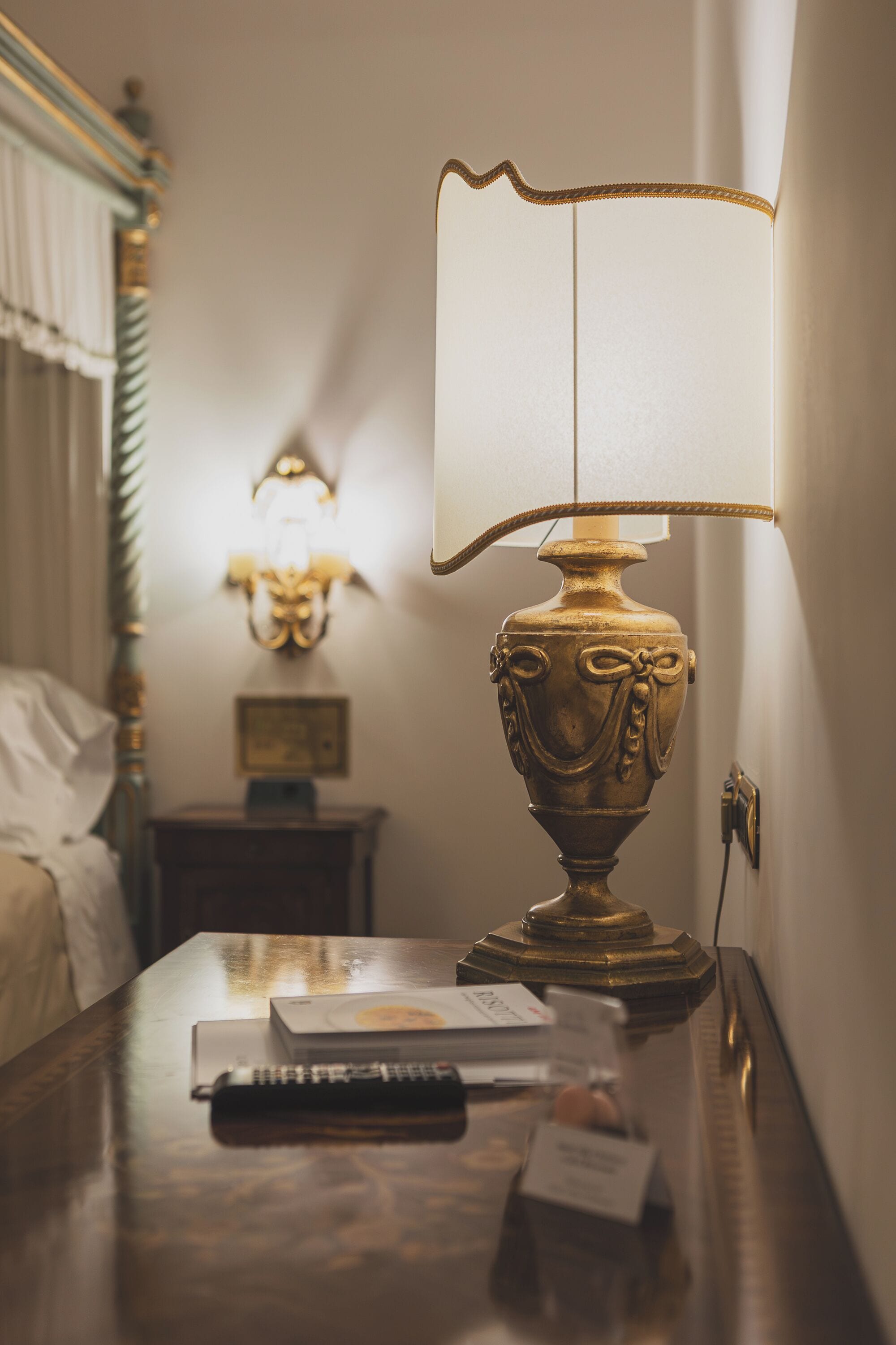 Quarto de hotel com uma cama, mesa de cabeceira com luminária, controle remoto e um cartão sobre a mesa.