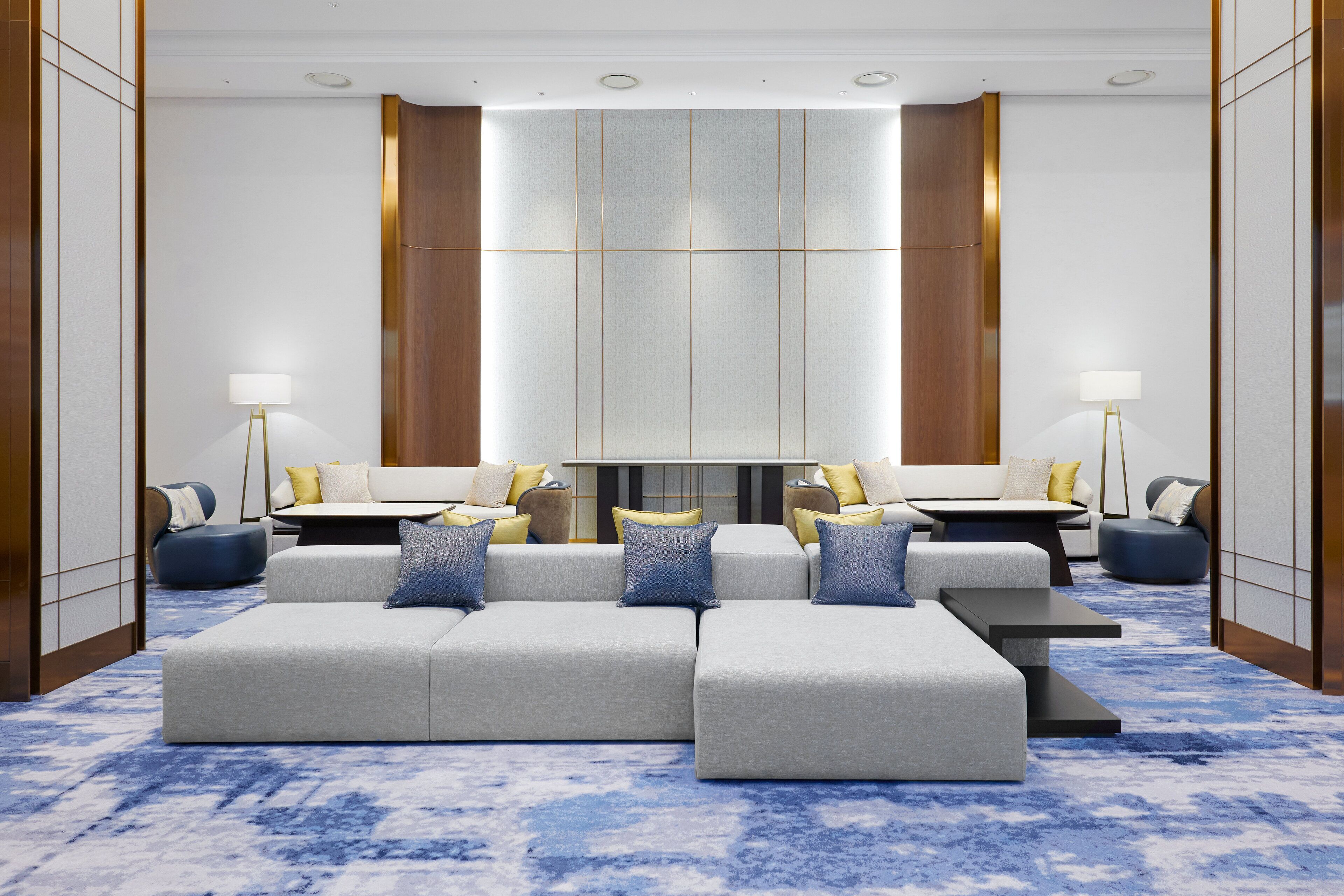 Um hall de hotel moderno com uma ampla área de estar, uma lareira e um tapete azul.