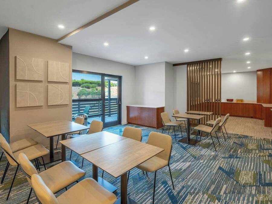 Quarto de hotel com uma janela grande, uma escrivaninha, uma cadeira, uma cama e um banheiro.