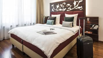 Quarto de hotel com uma cama grande, cabeceira de madeira e uma mala.