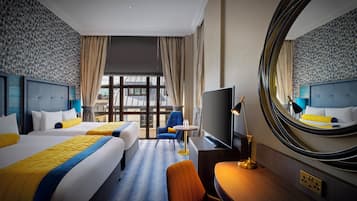 Quarto de hotel com duas camas, televisão, escrivaninha e um espelho grande.