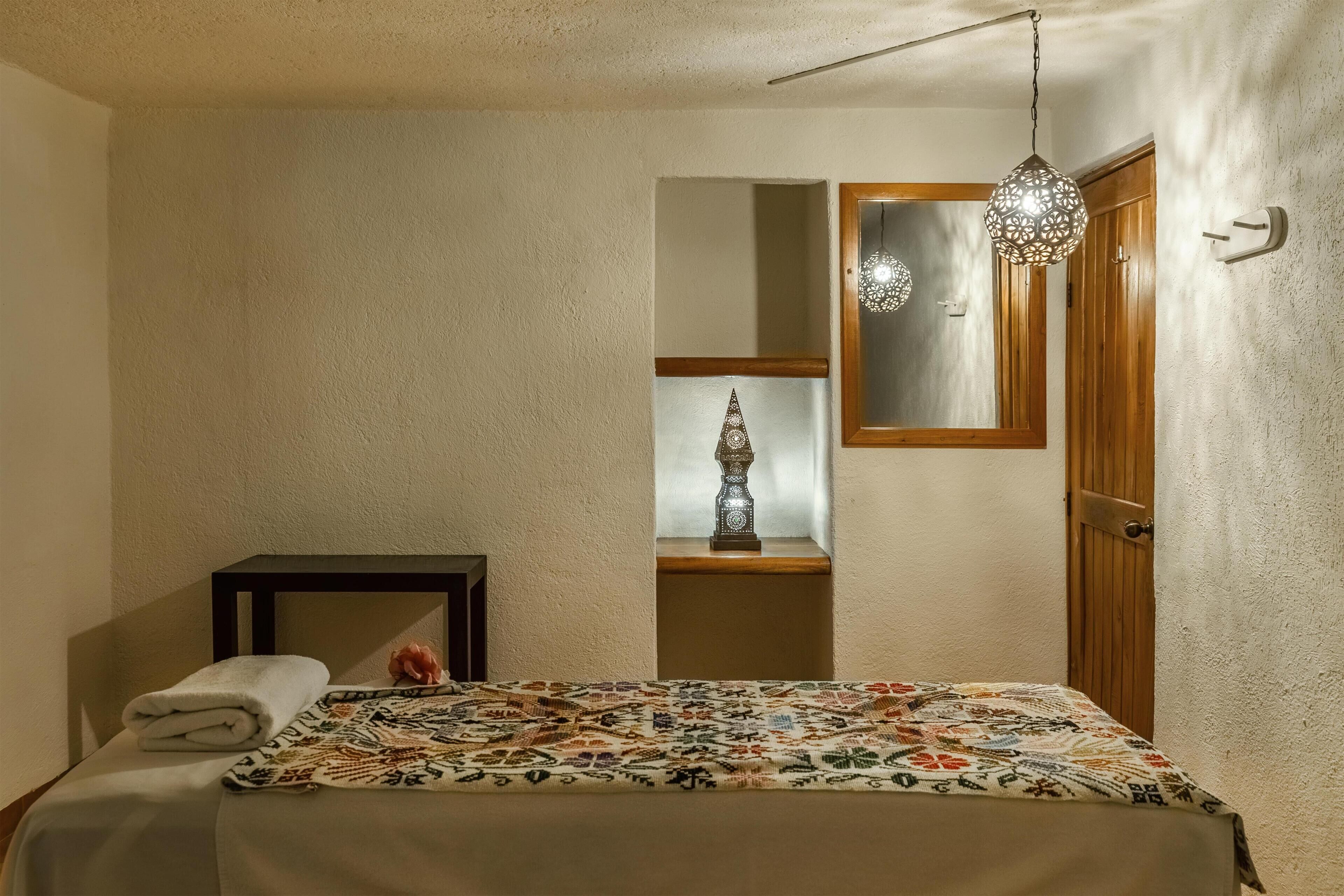 Quarto com cama, mesa de cabeceira, luminária, espelho e porta.
