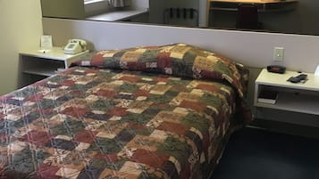 Quarto de hotel com cama grande, escrivaninha com telefone, espelho e mesinha de apoio com relógio e controle remoto.