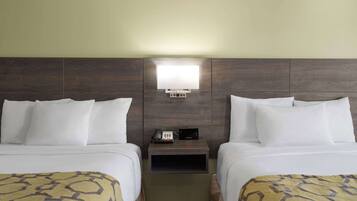 Quarto de hotel com duas camas, uma mesa de cabeceira com abajur e televisão presa na parede.