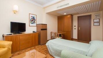 Quarto de hotel com uma cama, televisão, escrivaninha, cadeira, guarda-roupa e frigorífico.