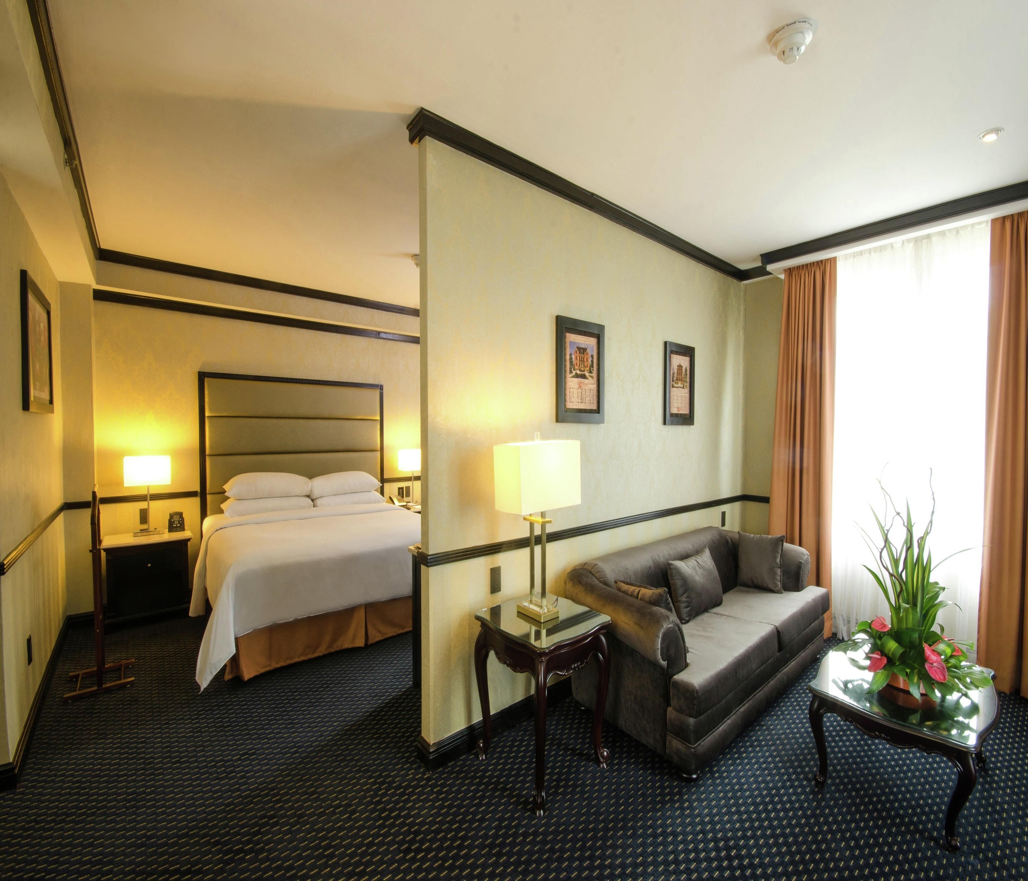 Quarto de hotel com cama, sofá, mesinha e abajur.