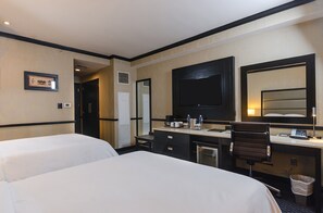 Quarto de hotel com duas camas, uma escrivaninha, uma cadeira, uma televisão e um cesto de lixo.