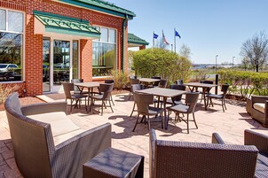Área de varanda externa com móveis de vime e um edifício de tijolos ao fundo.