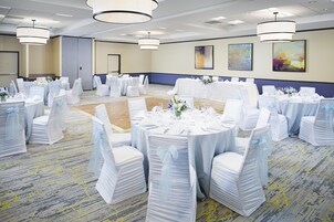 Uma sala de banquetes com mesas redondas, toalhas brancas e cadeiras com capas brancas.