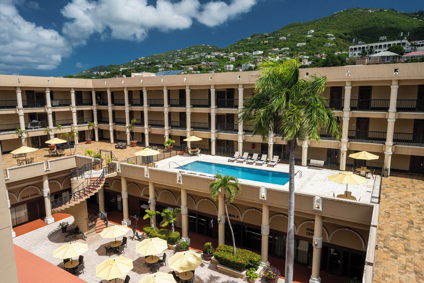 Um hotel com piscina central, área de estar externa e vários andares com varandas.