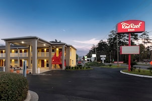 Um Red Roof Inn com um edifício de dois andares, área de estacionamento coberta e um letreiro vermelho.